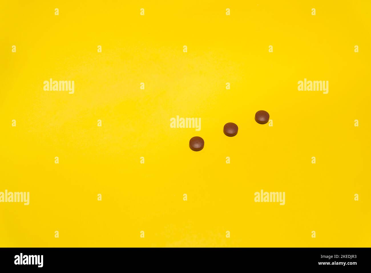 The three brown medical pills arranged isolated on a yellow background ...