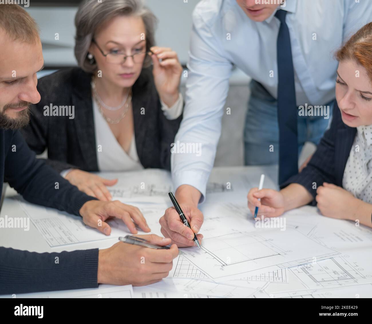 Four colleagues are discussing blueprints in a conference room in an ...