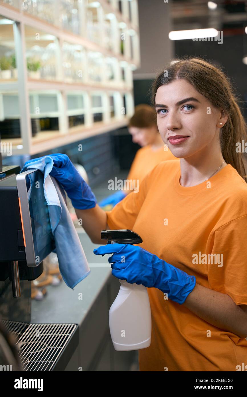 Smiling cleaning company employee washes coffee machine in coworking ...