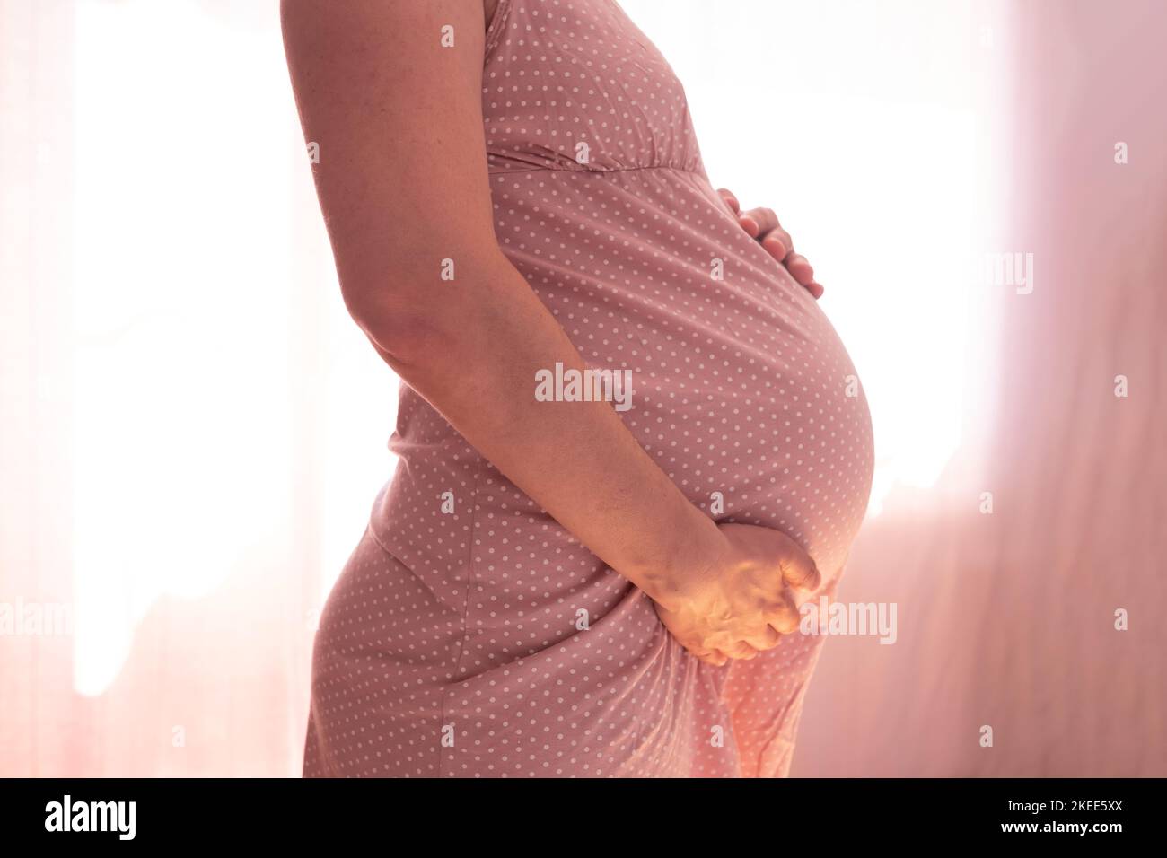 Pregnant woman touching belly standing near window Stock Photo - Alamy