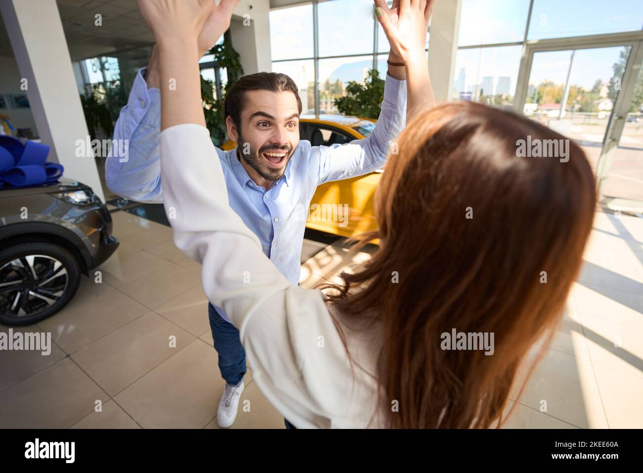 Cheerful young man and woman high-fiving each other in car showroom ...