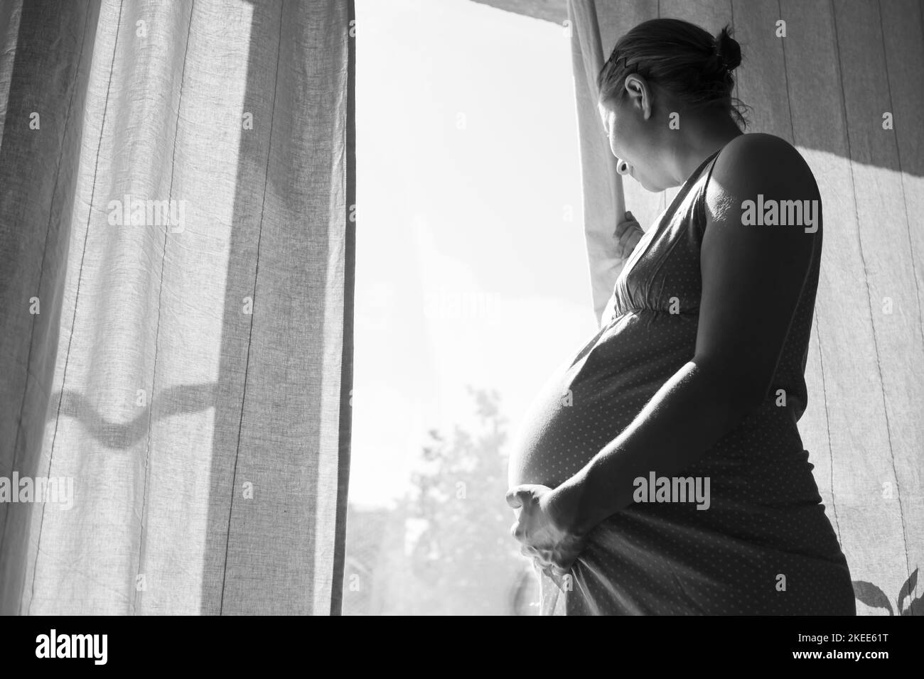 Pregnant woman touching belly standing near window Stock Photo - Alamy