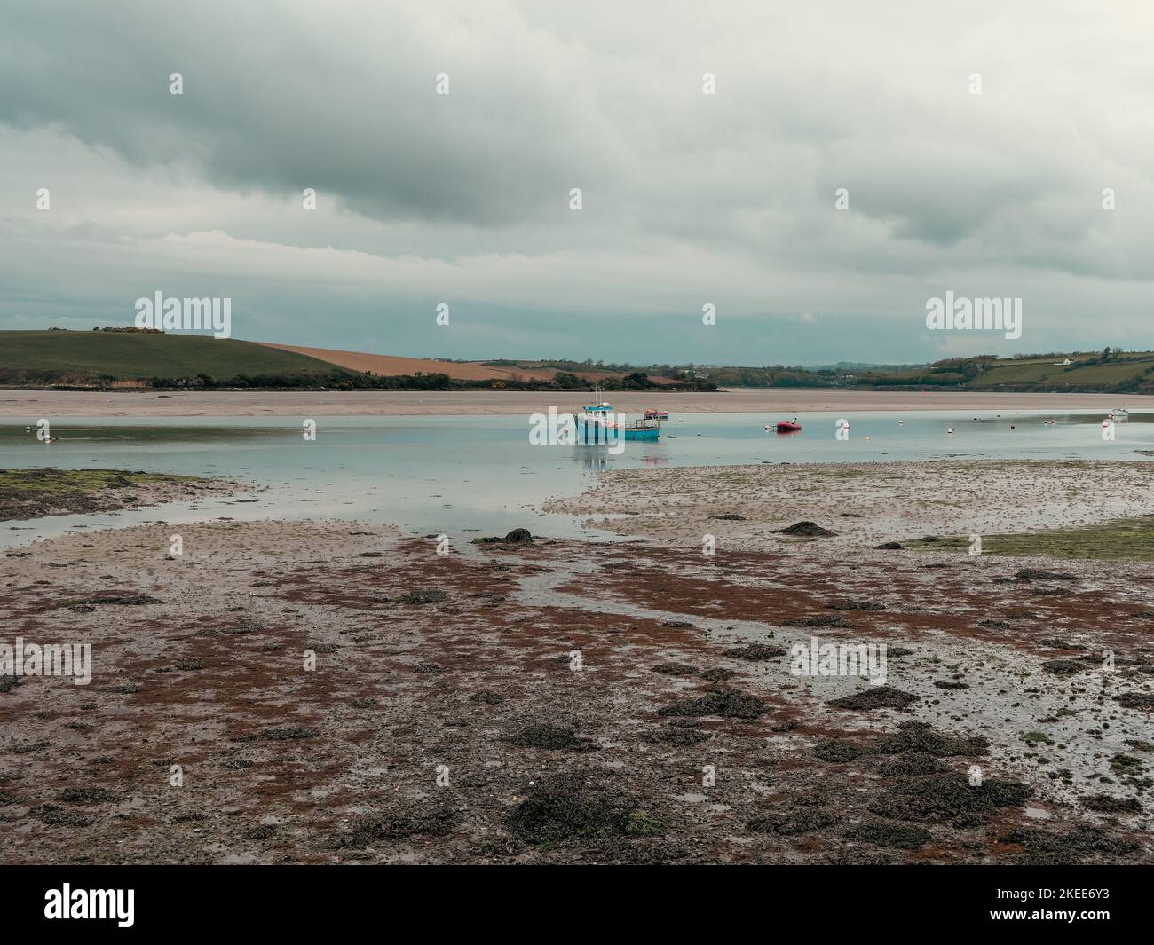 Clonakilty Bay at low tide on a day. A small blue fishing boat is ...