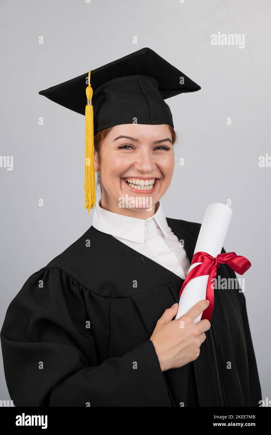 Smiling woman in graduation gown holding diploma on white background ...