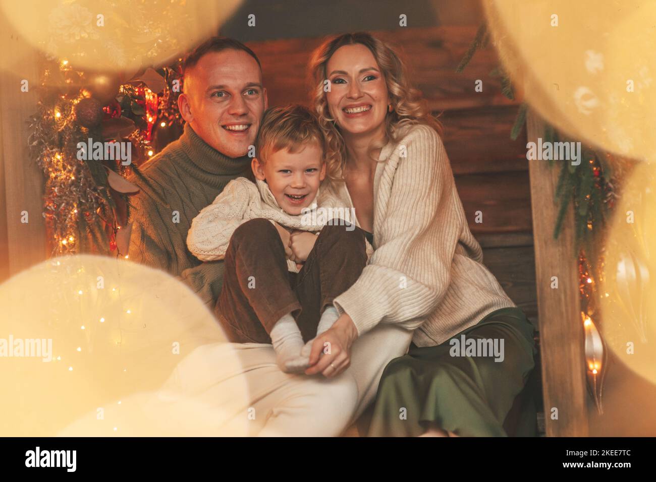 Portrait of happy family in knitted beige sweaters waiting Santa indoor ...