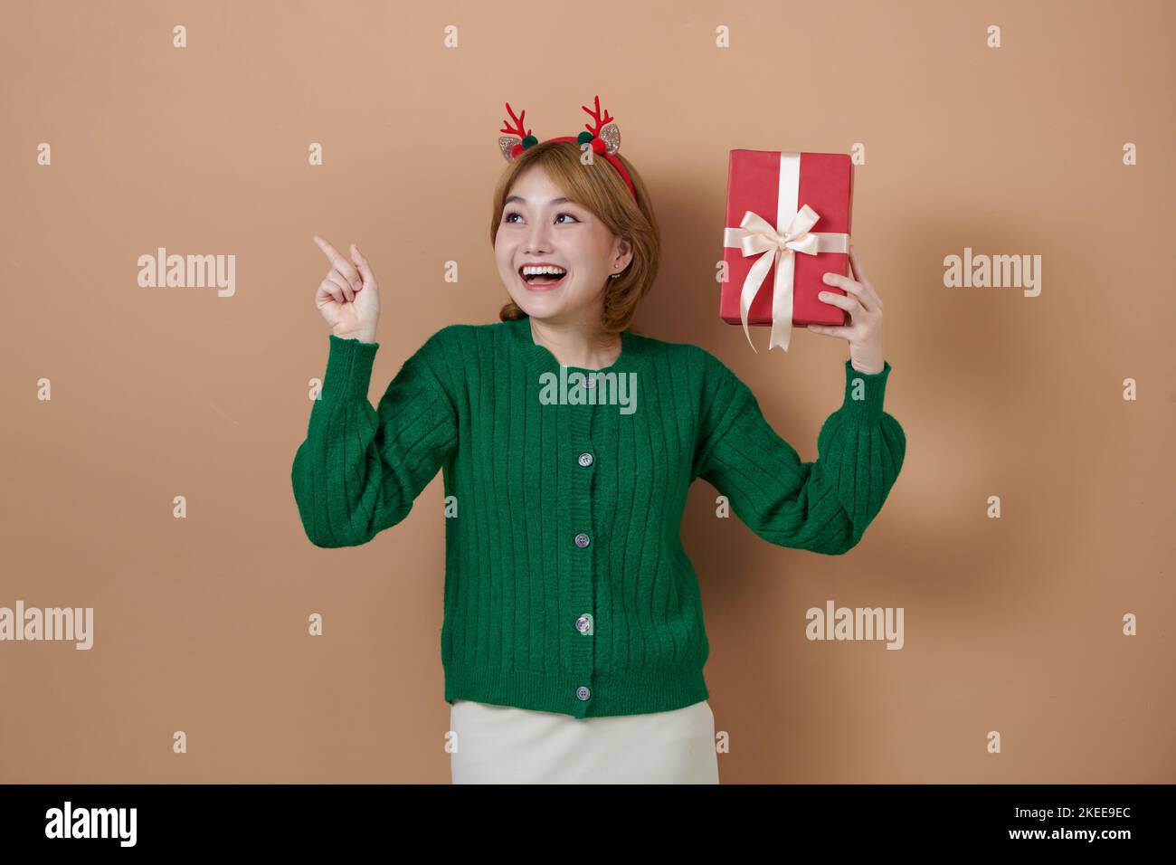 Happy girl wearing Christmas deer horns holding a gift box, pointing to ...