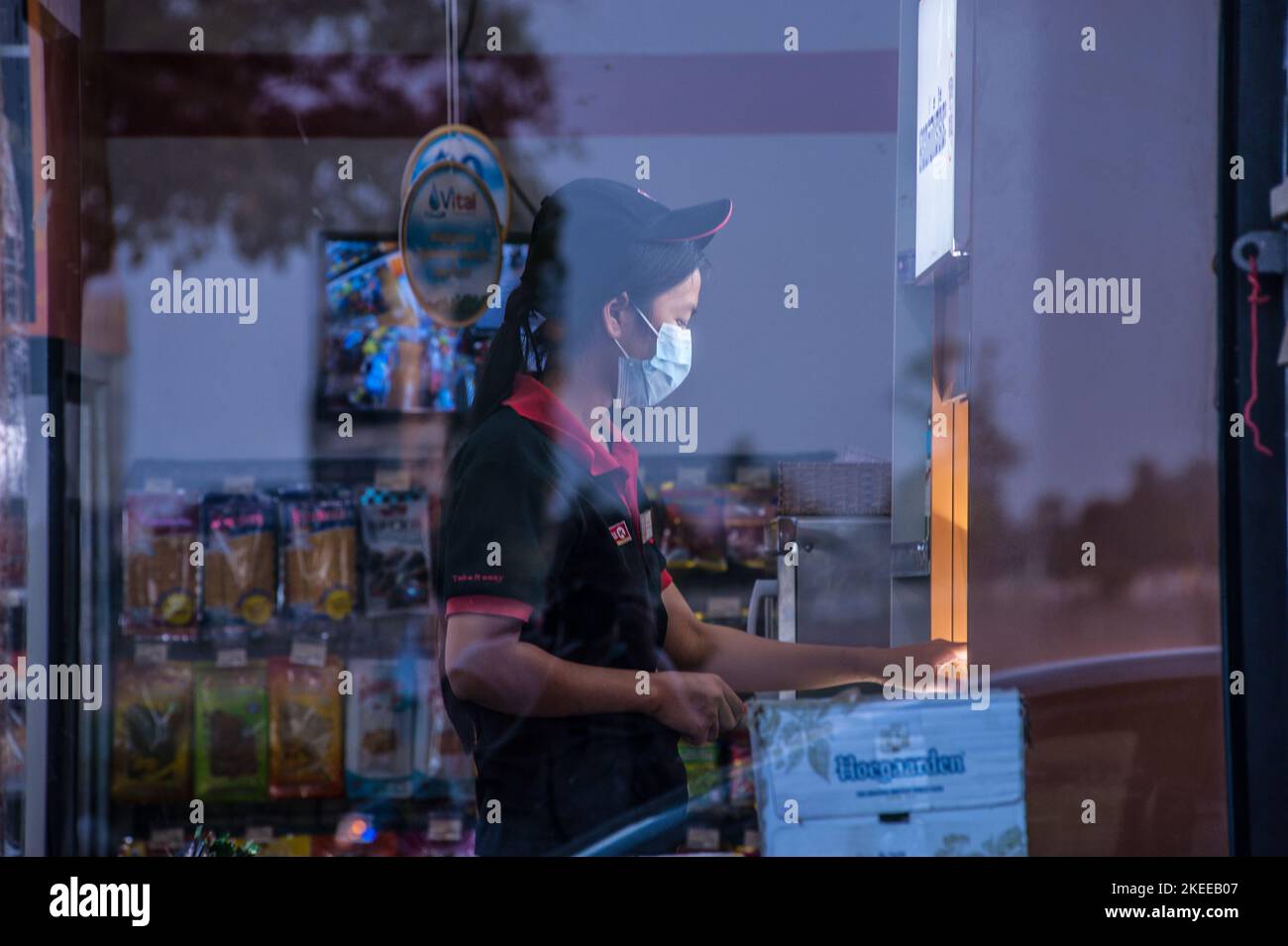 A convenience store female employee, wearing a face mask, working on ...