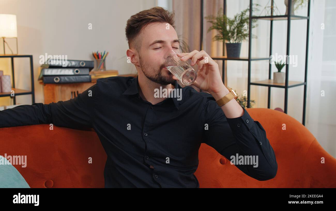 Portrait of thirsty lovely man sitting indoors holding glass of natural ...