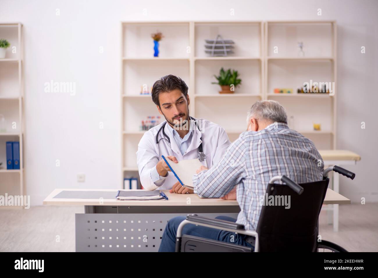 Old male patient in wheelchair visiting young male doctor Stock Photo ...