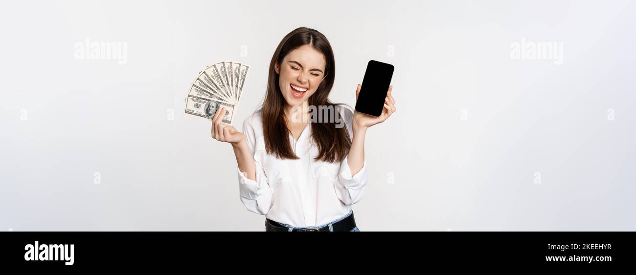 Enthusiastic young woman winning money, showing smartphone app ...