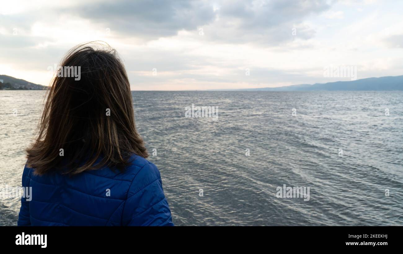 Middle aged woman standing alone and looking to the sea. Thinking ...