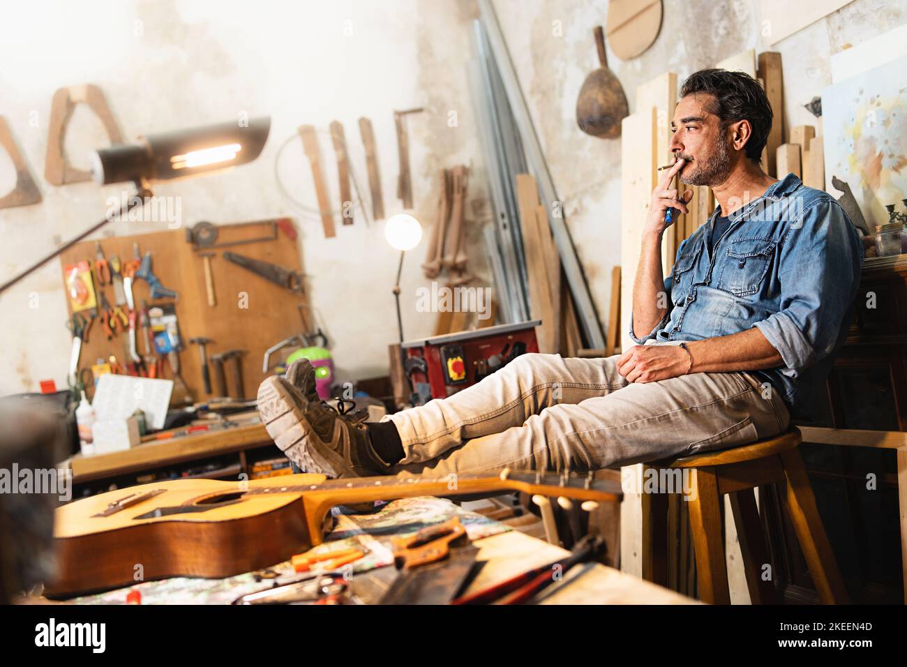 A carpenter relaxes sitting on a stool by placing his feet on the work ...