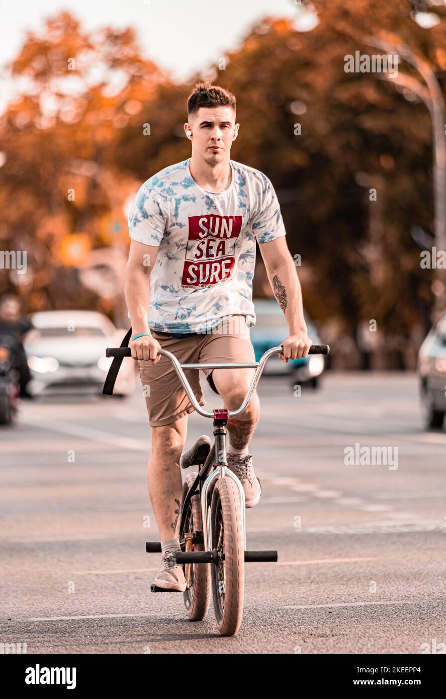 A vertical of a Caucasian guy riding a bicycle BMX on the street in ...