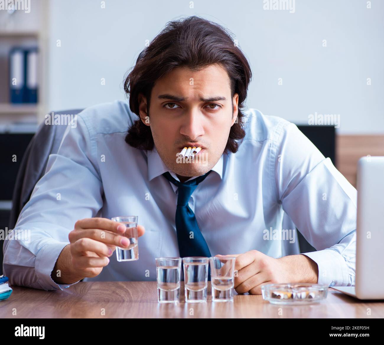 The male employee drinking vodka and smoking cigarettes at workplace ...
