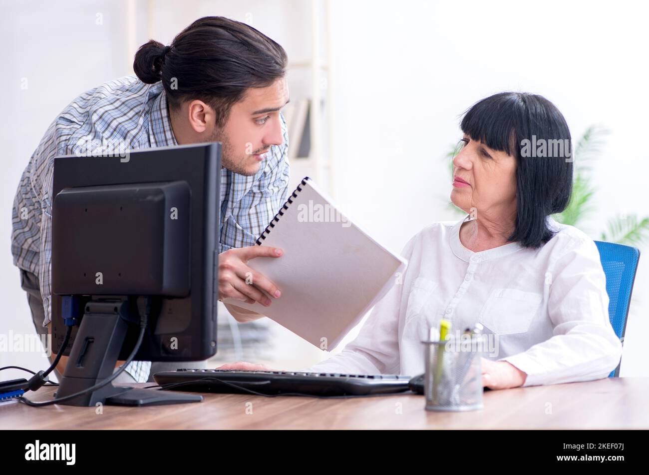 Young male employee explaining to old female colleague how to use ...