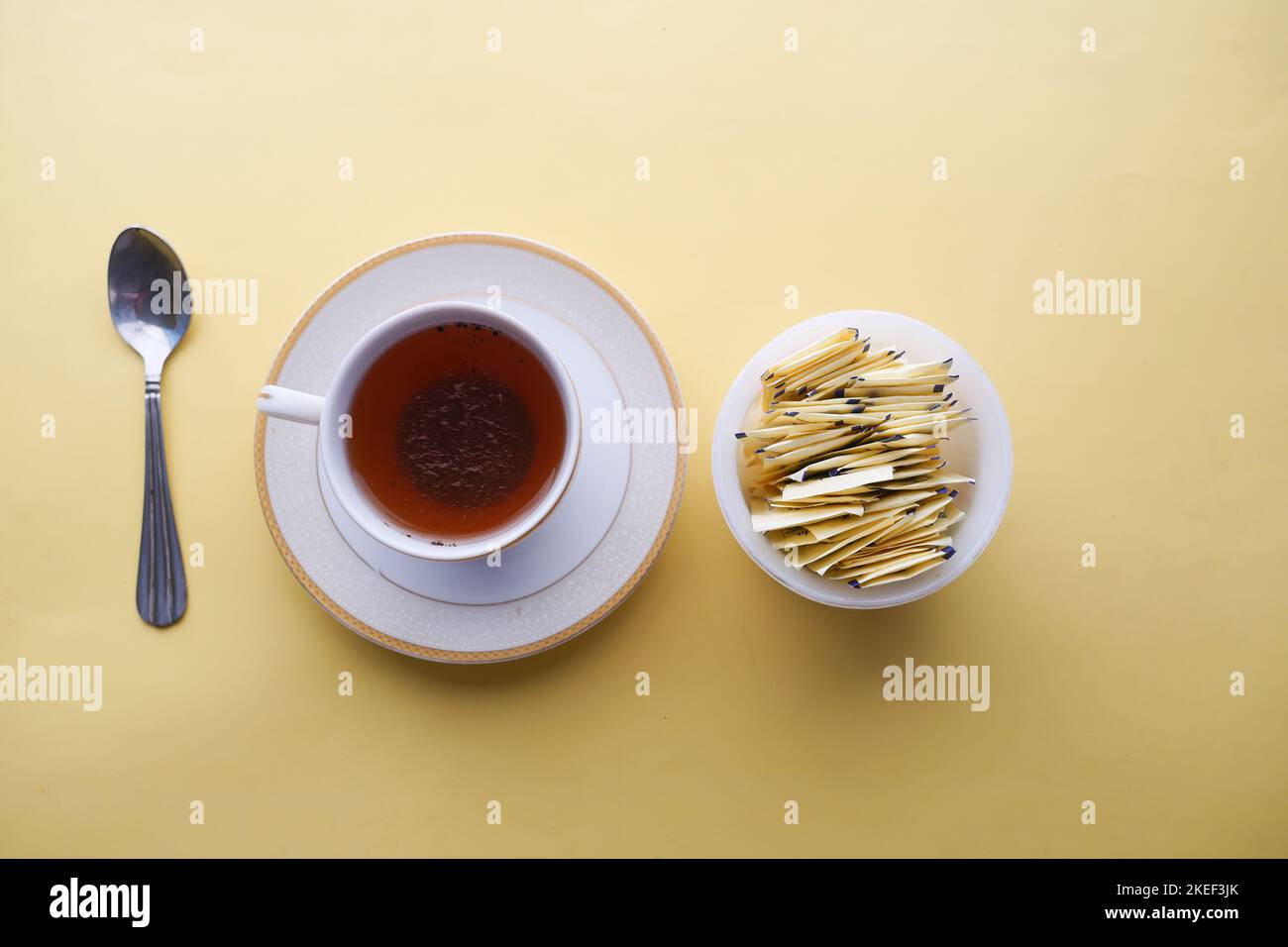 artificial sweetener powder in a packet and cup of tea on yellow ...