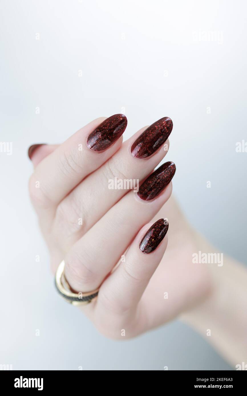 Woman hand with long nails and a bottle of dark red burgundy nail ...