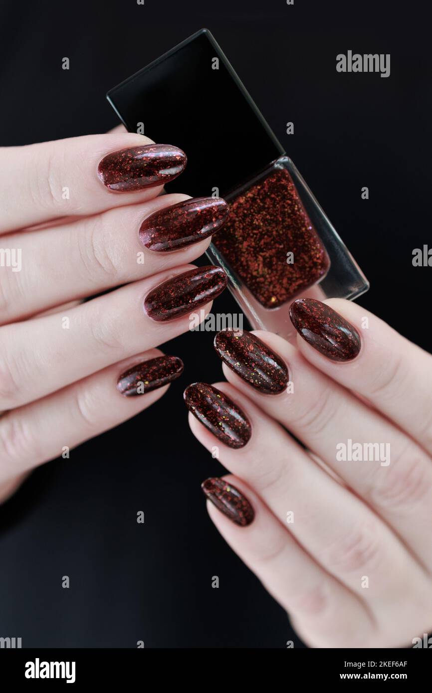 Woman hand with long nails and a bottle of dark red burgundy nail ...