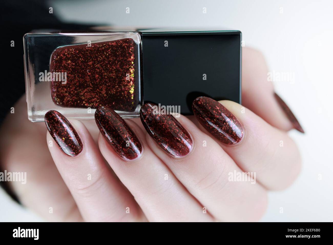 Woman hand with long nails and a bottle of dark red burgundy nail ...