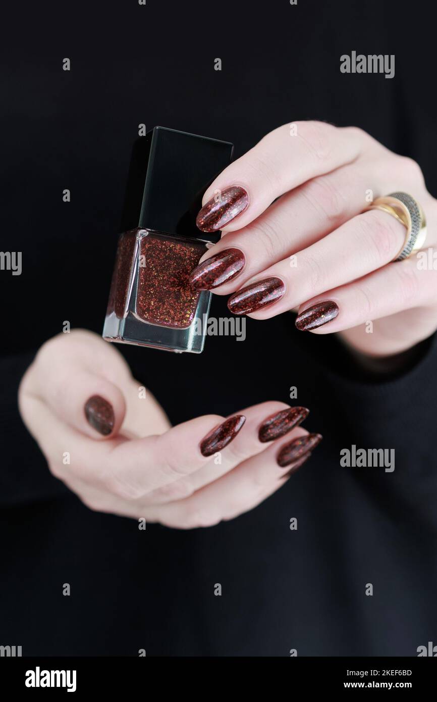 Woman hand with long nails and a bottle of dark red burgundy nail ...
