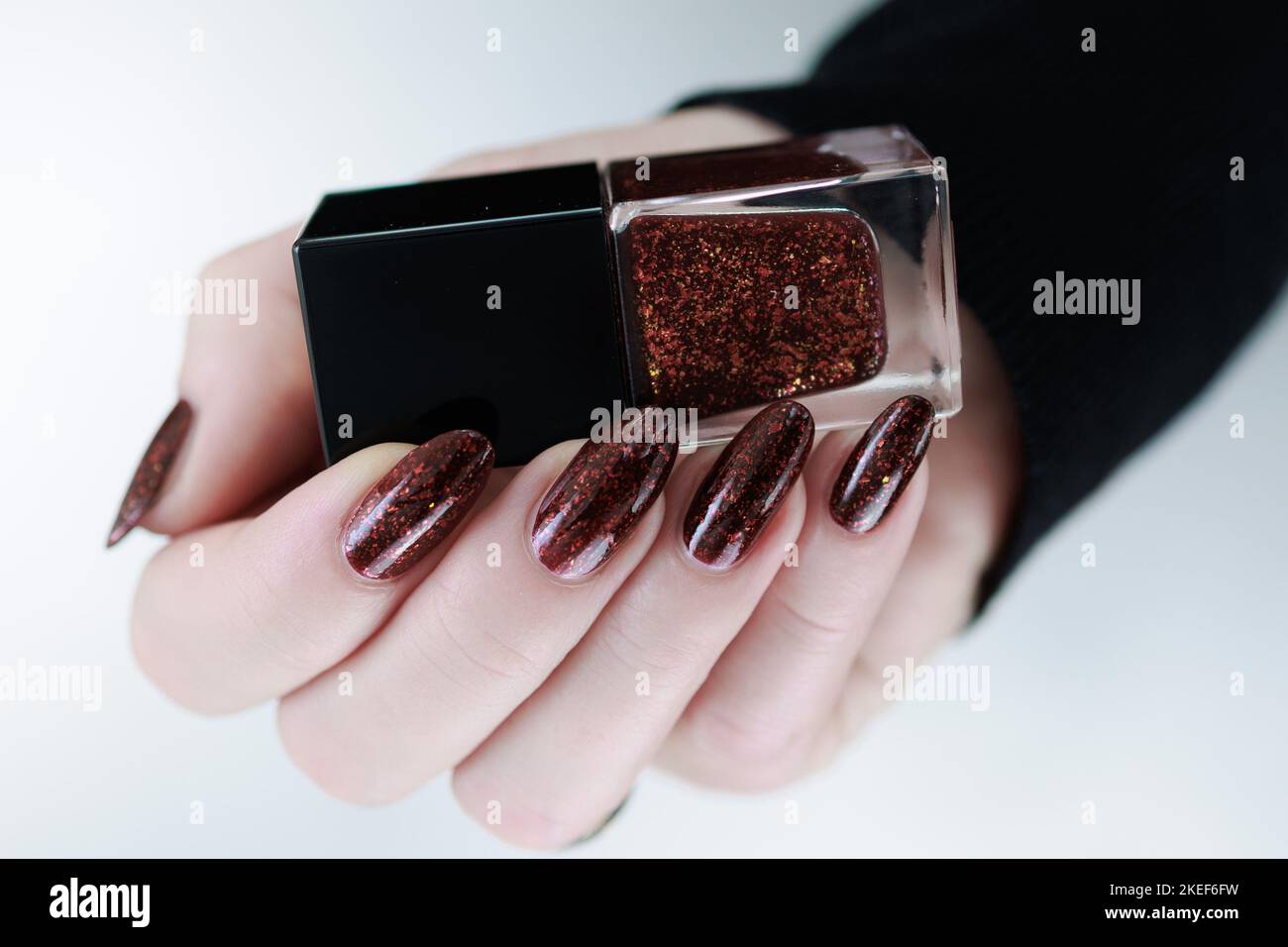 Woman hand with long nails and a bottle of dark red burgundy nail ...