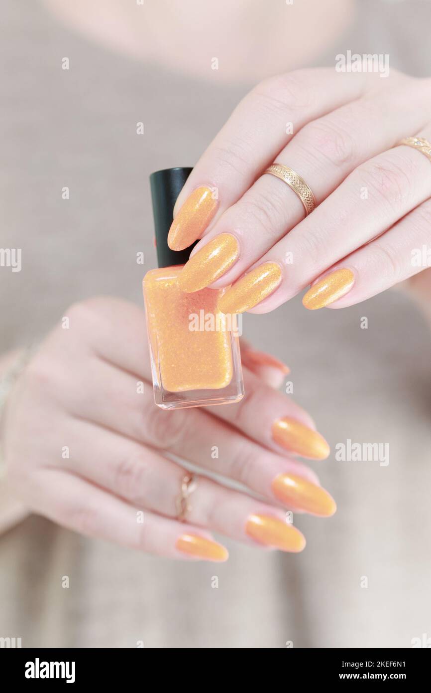 Woman's hands with long nails and a bottle of orange nail polish Stock ...