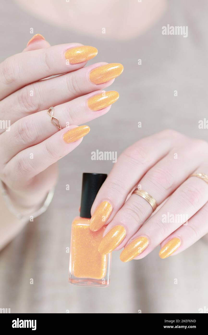 Woman's hands with long nails and a bottle of orange nail polish Stock ...