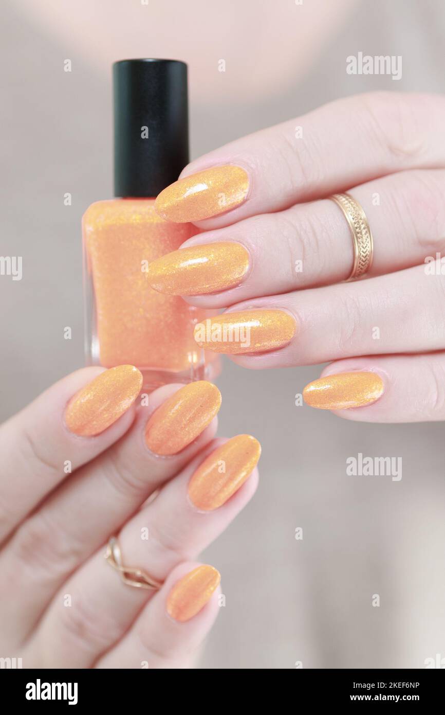 Woman's hands with long nails and a bottle of orange nail polish Stock ...