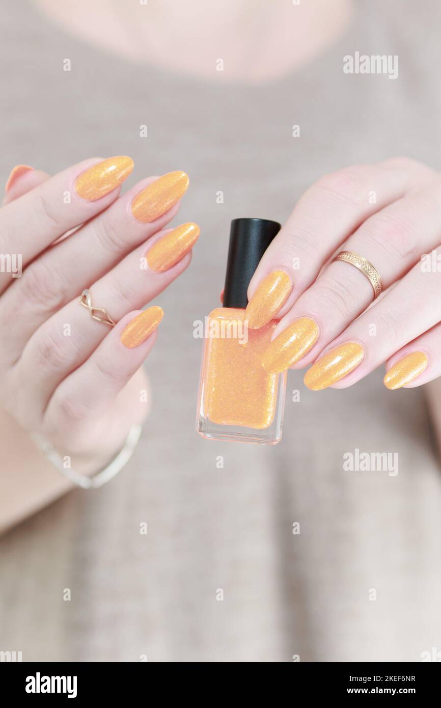 Woman's hands with long nails and a bottle of orange nail polish Stock ...