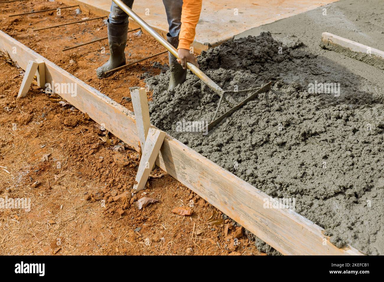 Workers pour cement around house on side of building to create an ...