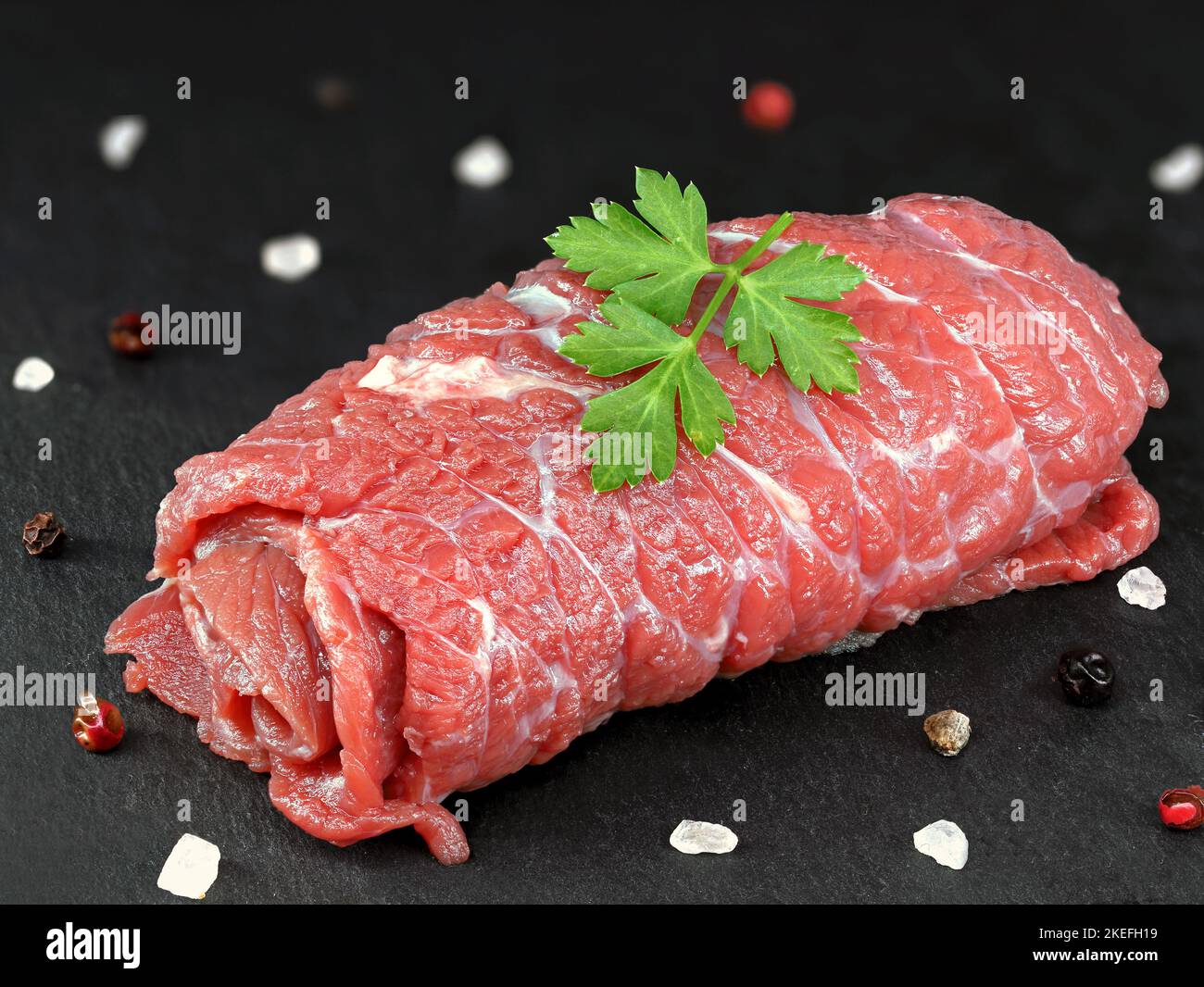 single raw unfilled beef roulade with salt and peper on black slate ...