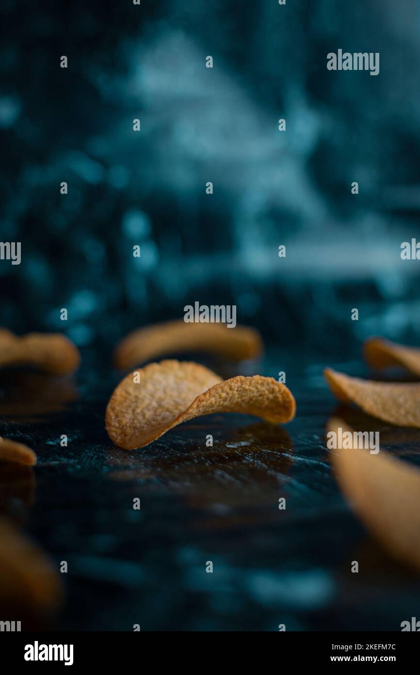 A vertical closeup shot of rounded potato chips on a dark blue surface ...