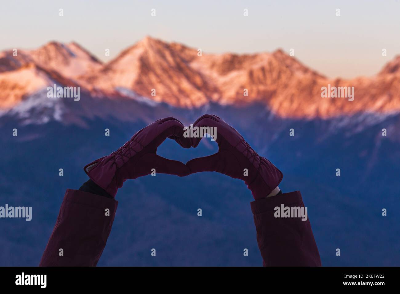Woman making heart shape with hands over snowy mountains in the winter ...