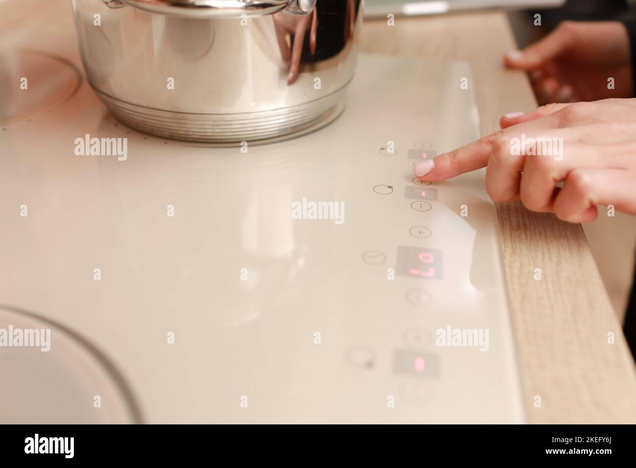 Female hand turns on electric hob closeup, finger presses sensor button ...