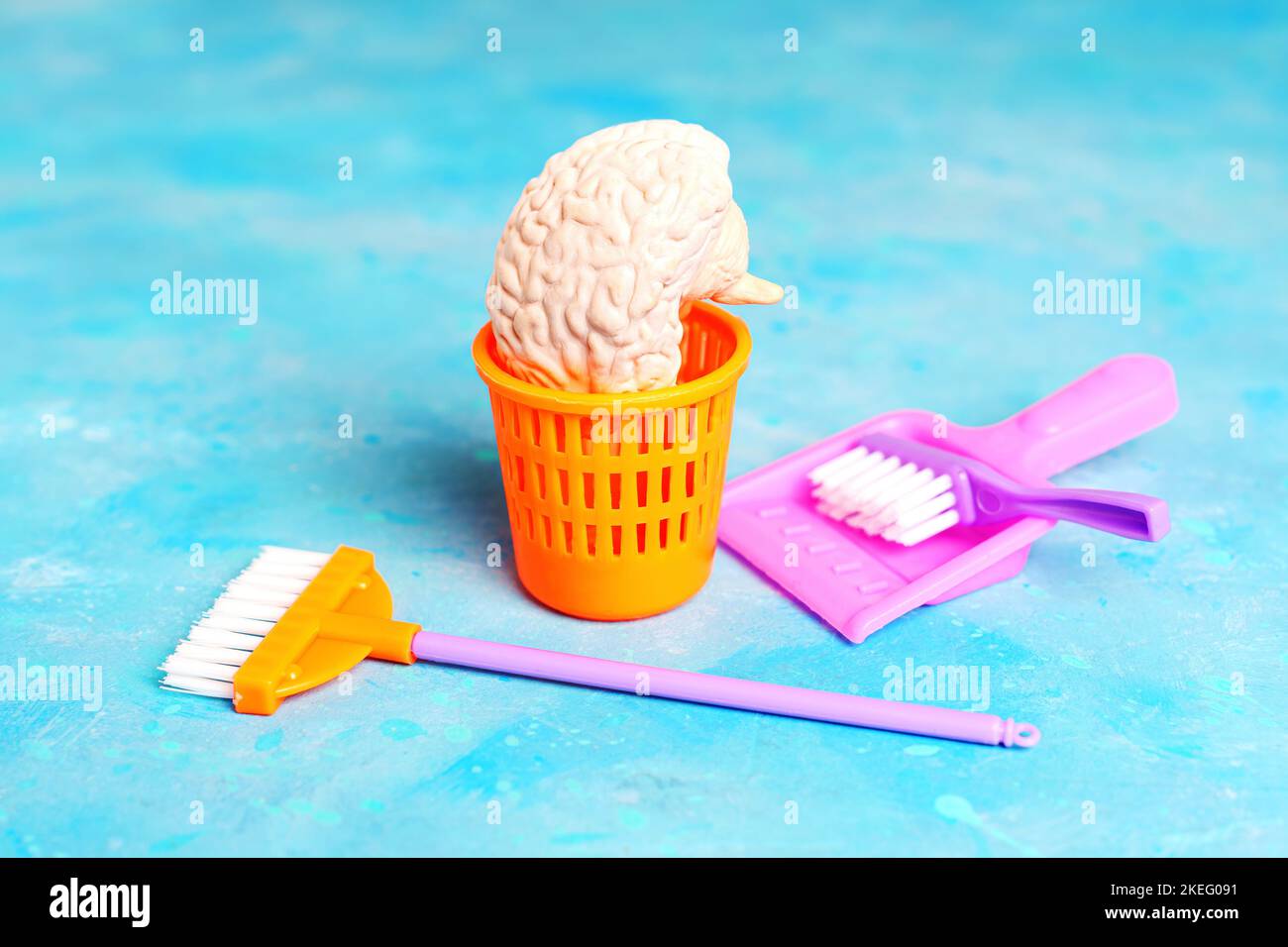Human brain in trash can and toy home cleaning tools arranged on blue ...