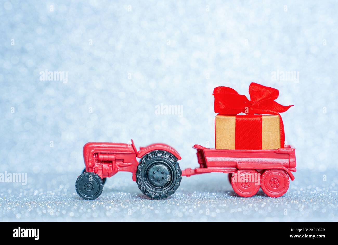 Greeting card: red toy tractor carries a large wrapped gift box against ...