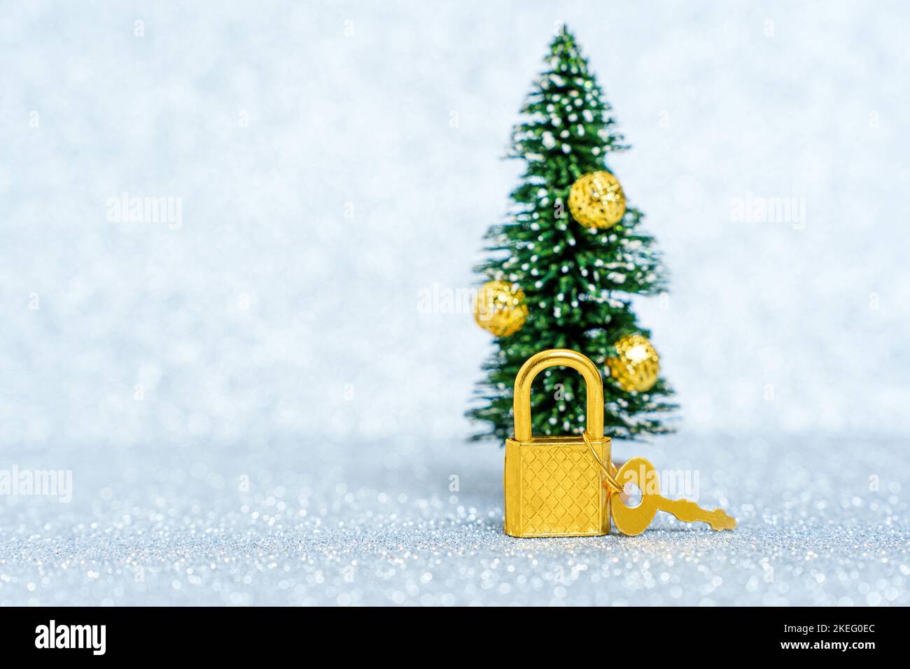 Small keyed padlock placed in front of a miniature toy Christmas tree ...