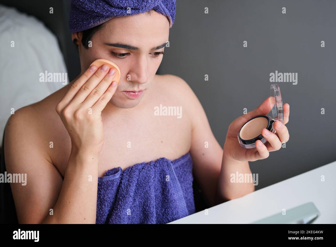 Young transgender man applying make-up base after shower Stock Photo ...