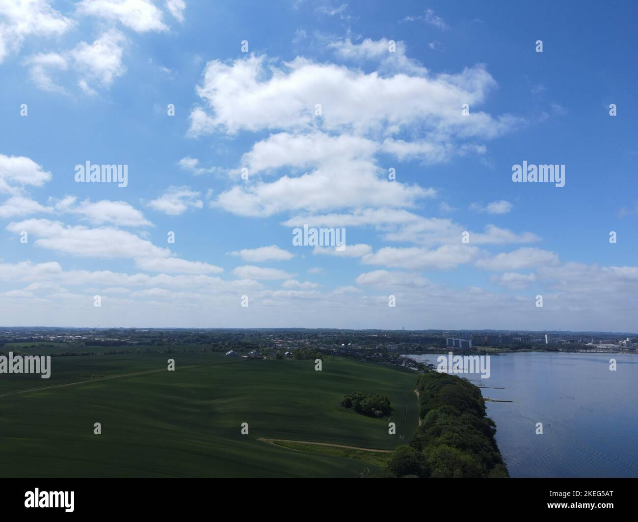 An aerial view of a calm river with green trees and a cloudy blue sky ...