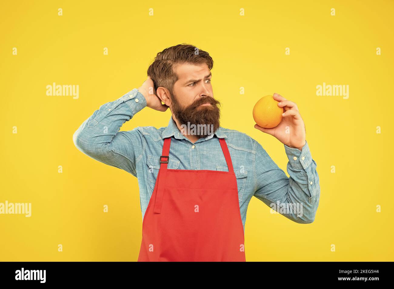 Puzzled man in apron looking at fresh orange fruit scratching head ...