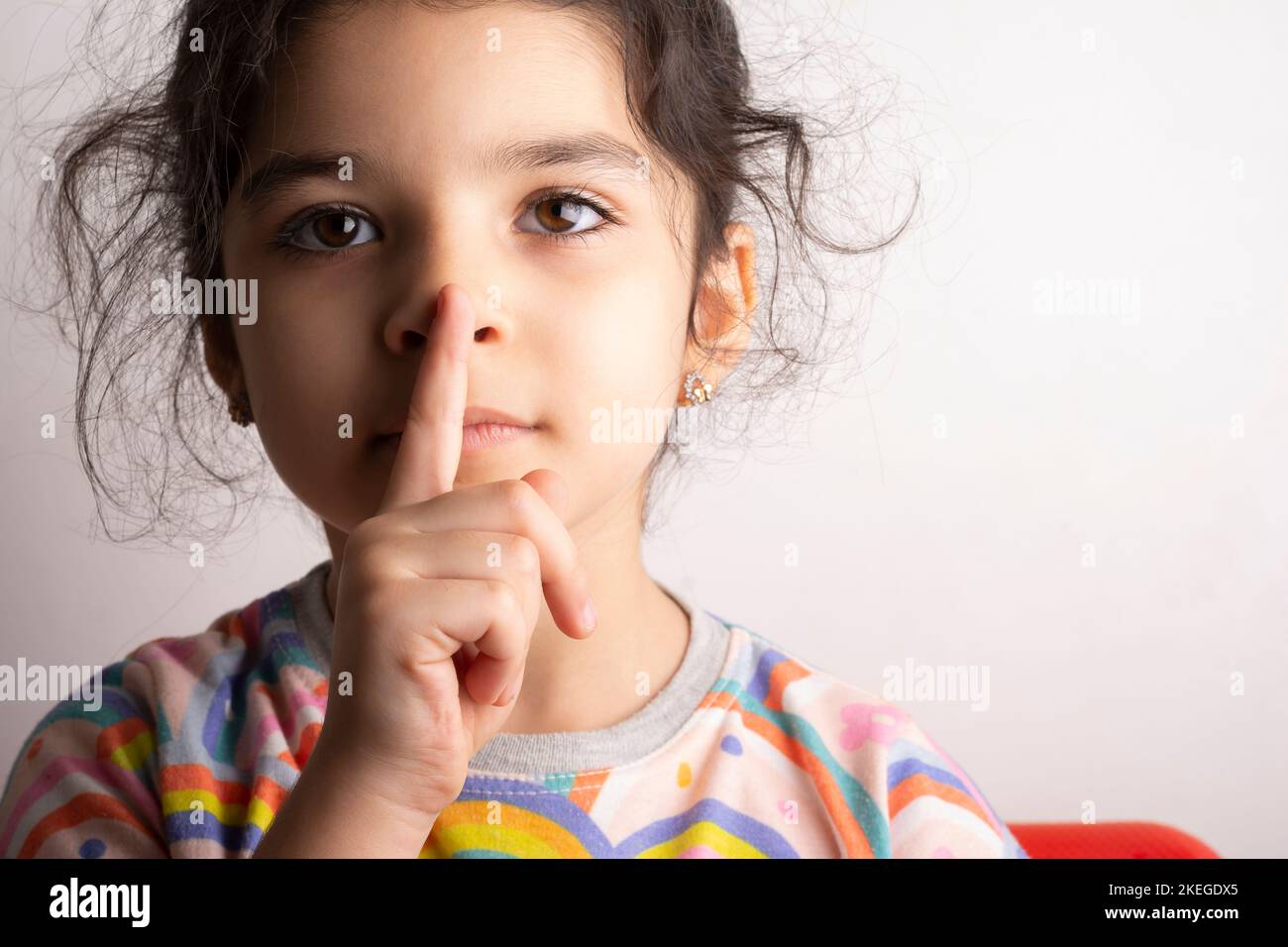 Portrait of a little girl showing sign to be silent - keeping secret ...