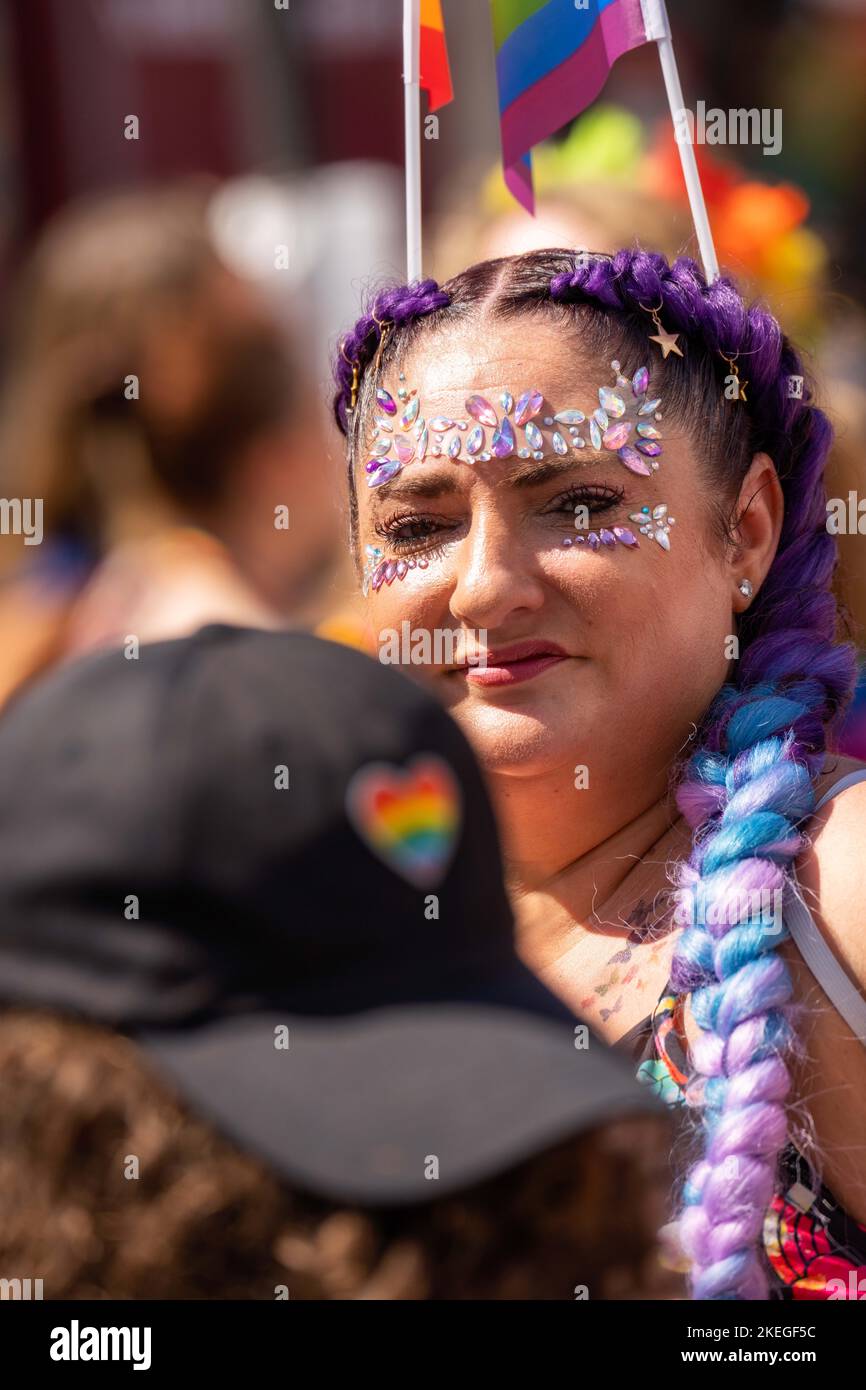 A vertical closeup of a woman with colored hair and pride flags on her ...
