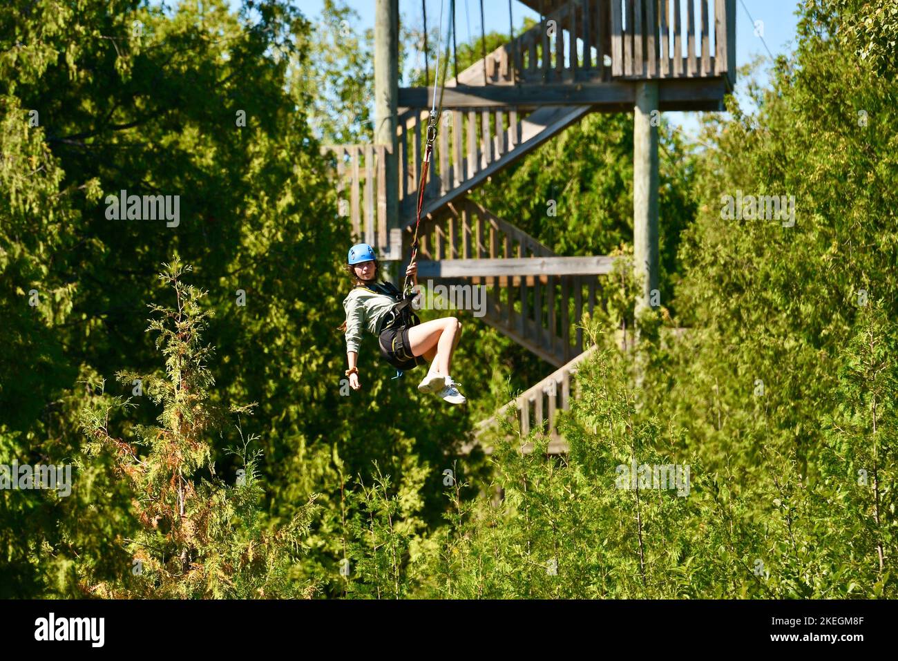 Beautiful cute young woman gliding through forest canopy with Lakeshore ...