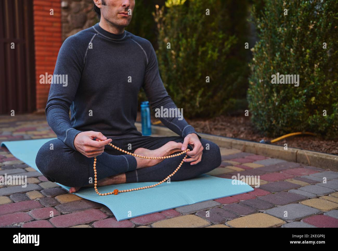 Cropped view of a yogi sitting on a fitness mat, meditating with rosary ...