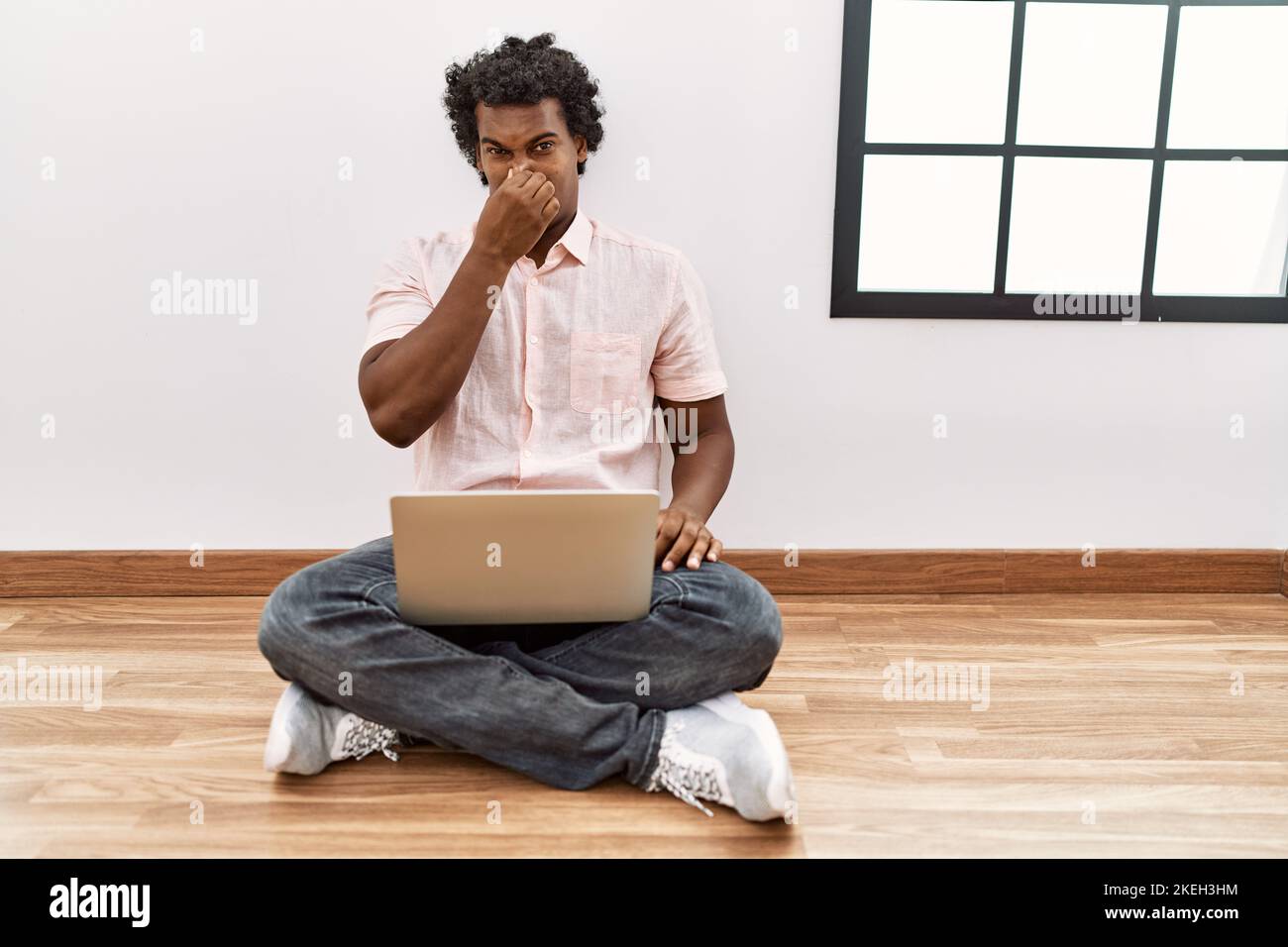 African man with curly hair using laptop sitting on the floor smelling ...