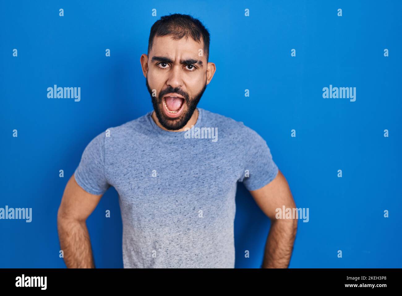 Middle east man with beard standing over blue background angry and mad ...