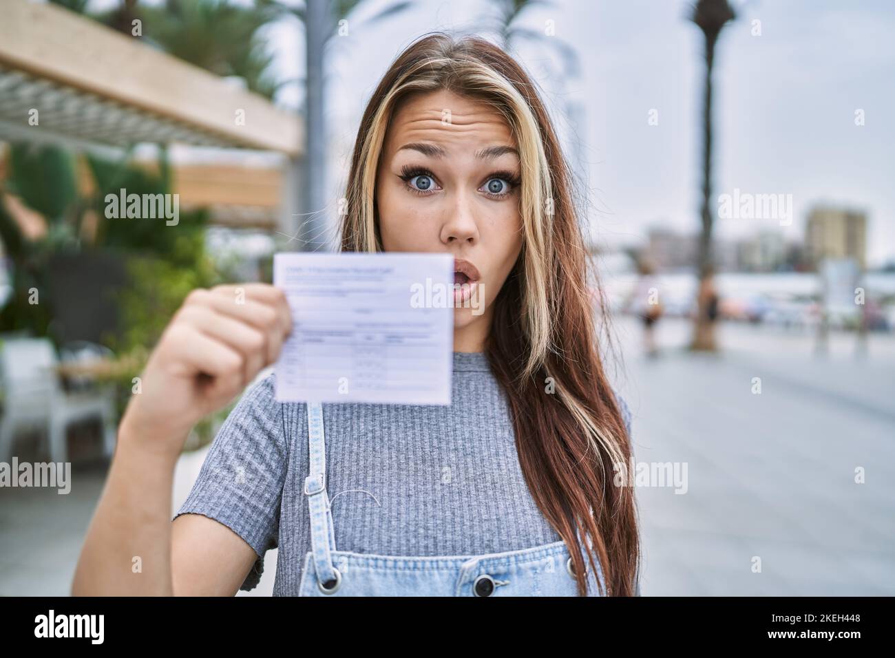 Young caucasian woman holding covid record card scared and amazed with ...
