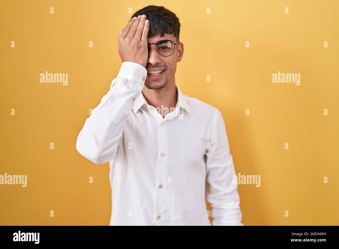 Young hispanic man standing over yellow background covering one eye ...