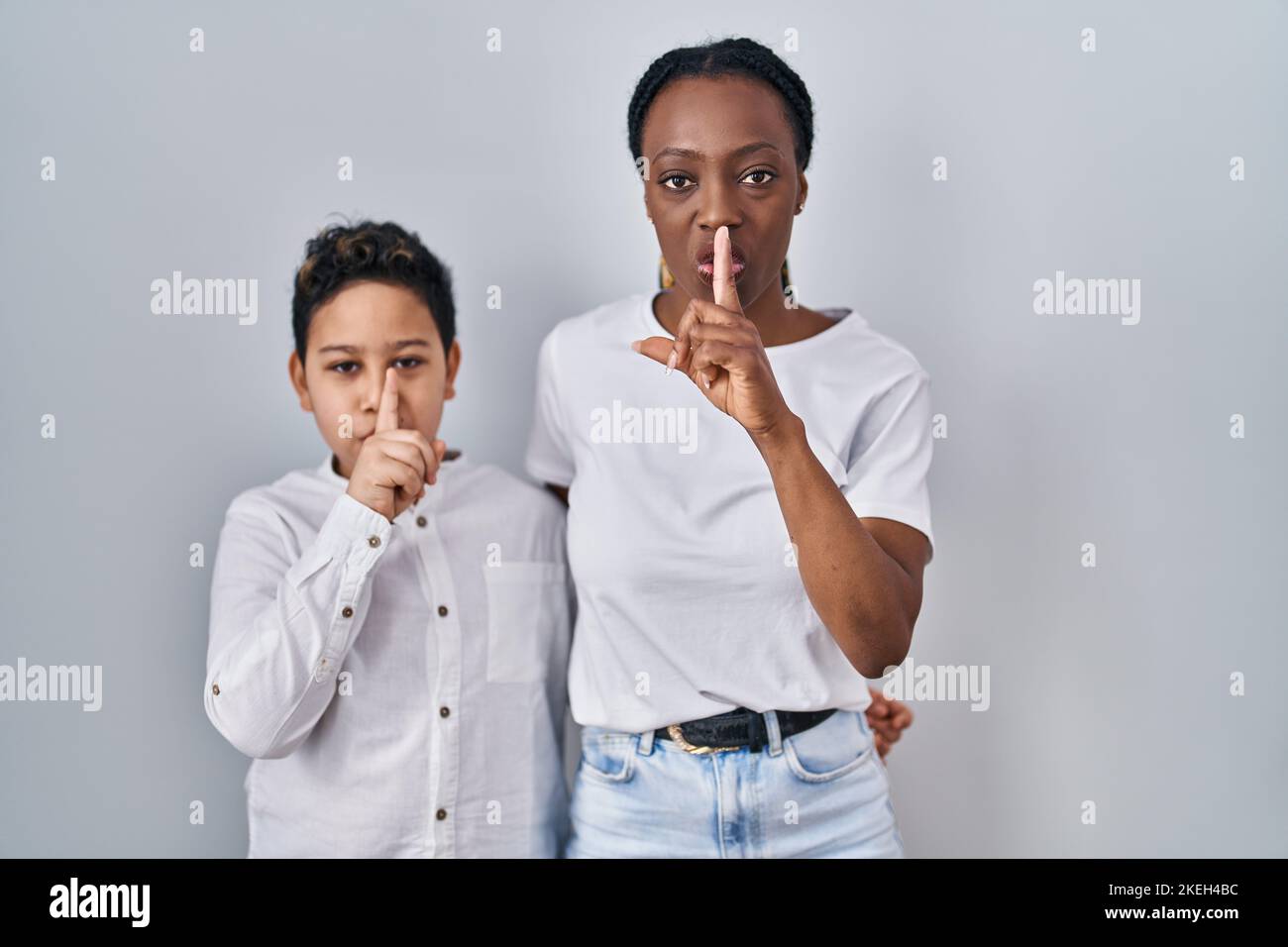 Young mother and son standing together over white background asking to ...