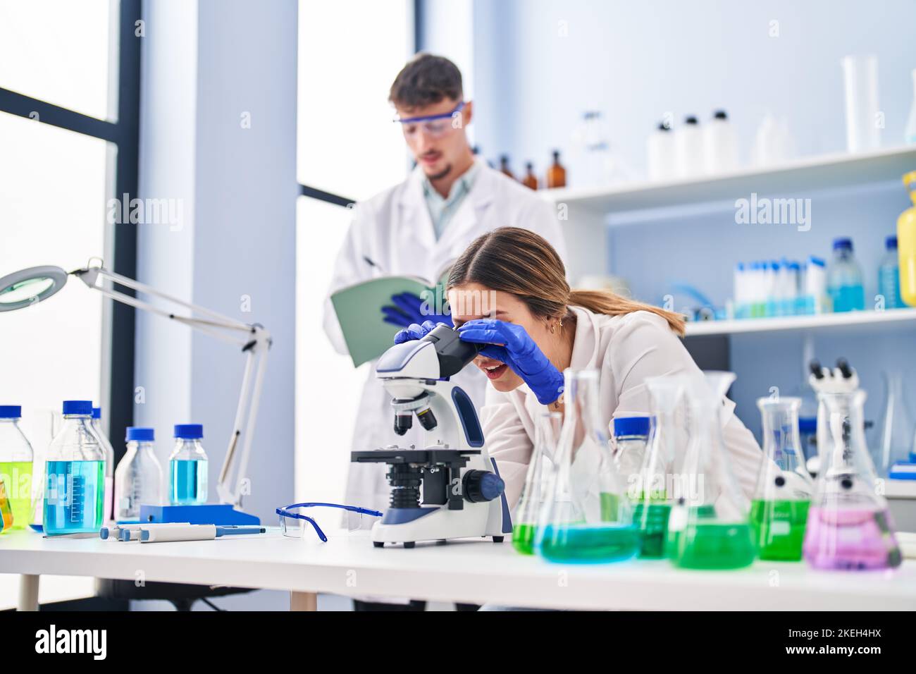 Young man and woman scientists workers using microscope at laboratory ...